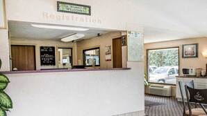 Uma área de recepção com balcão de registro, um pequeno espaço de espera e uma janela com vista para carros estacionados lá fora.