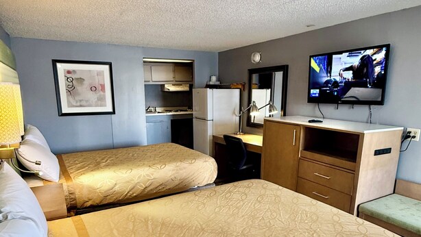 Quarto de hotel com duas camas, uma escrivaninha, televisão e uma kitchenette.