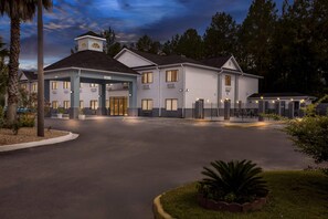 Hotel com vários andares, entrada coberta e área de estacionamento cercada.