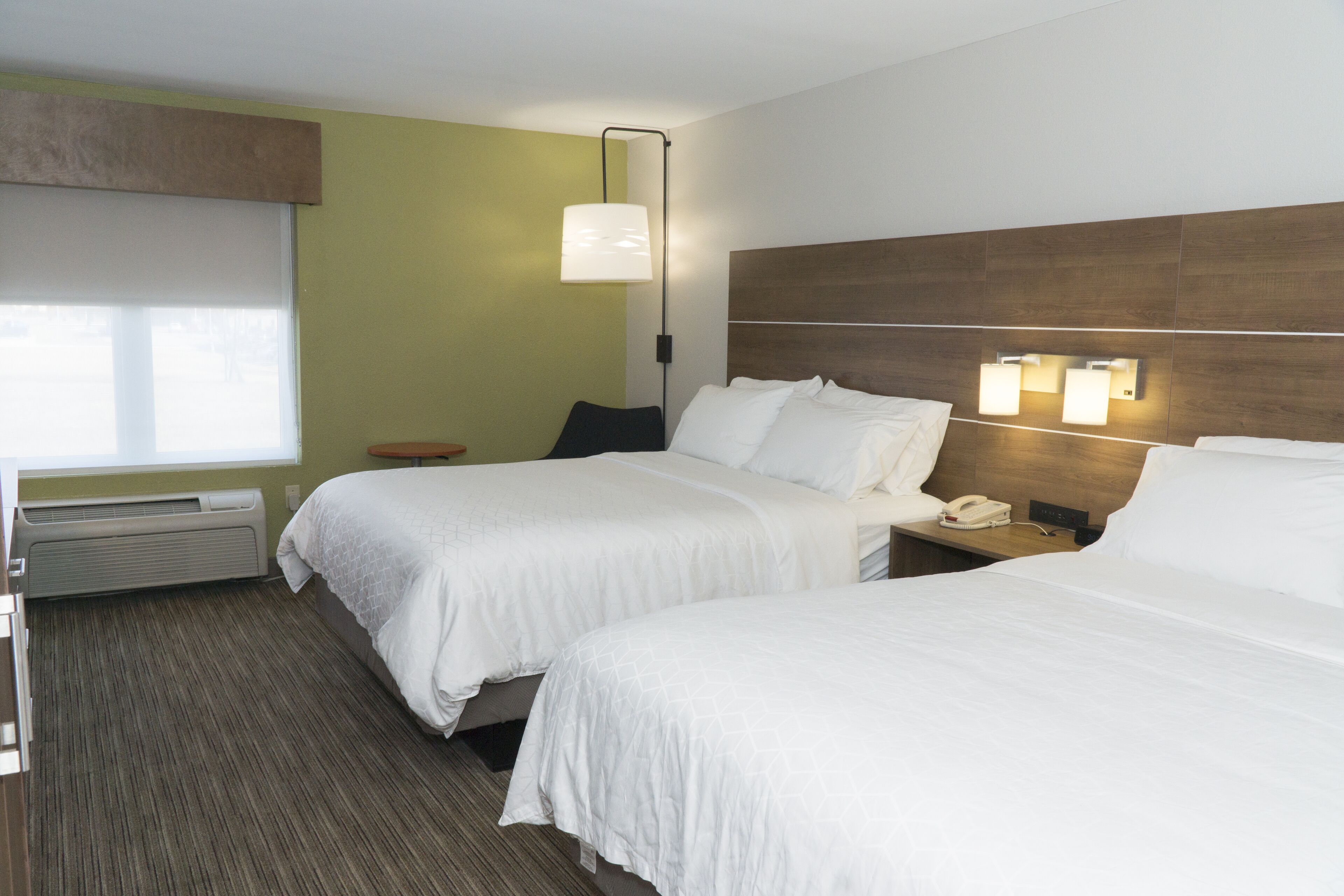 Quarto de hotel com duas camas, uma mesa de cabeceira com abajur, telefone e luminária na parede.