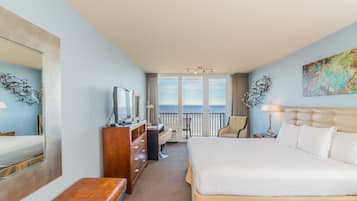 Quarto de hotel com uma cama grande, uma escrivaninha com computador, televisão e varanda com vista para o mar.
