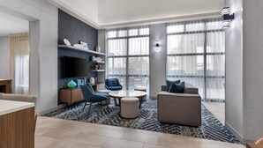 Uma sala de estar moderna com televisão de tela plana, assentos confortáveis, uma mesa de centro e uma janela grande com cortinas leves.