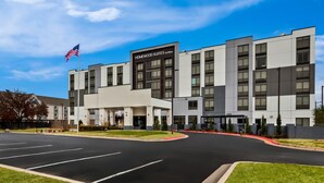 Um hotel moderno com uma placa grande indicando "HOMEWOOD SUITES by Hilton" e um mastro com a bandeira americana.