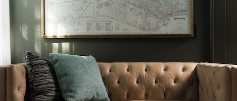 Quarto com sofá estofado, mesa de centro redonda de madeira e um mapa emoldurado na parede.