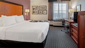 Quarto de hotel com uma cama grande, uma escrivaninha com cadeira, penteadeira, televisão e janela com cortinas.