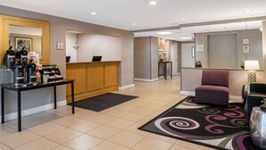 Um saguão de hotel com balcão de recepção, espaço para café, área de estar e um tapete decorativo.