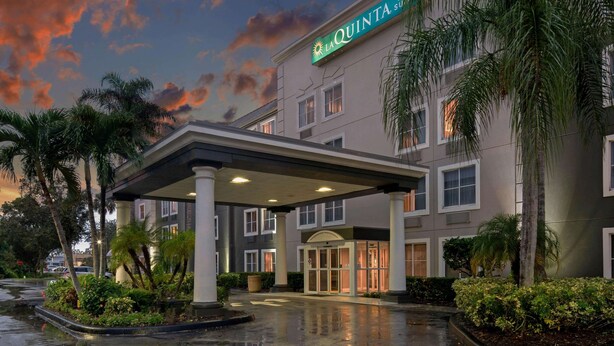 Entrada de hotel com área coberta, palmeiras e uma placa com a inscrição "LA QUINTA".