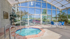 Uma área de piscina com paredes de vidro, incluindo uma banheira de hidromassagem, uma mesa com cadeiras e vista para o estacionamento.