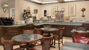 Uma cozinha de hotel com uma ilha central, banquetas de bar e uma área de refeições com mesas e cadeiras redondas.