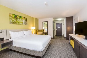 Quarto de hotel com uma cama grande, mesa de cabeceira, luminária e televisão.