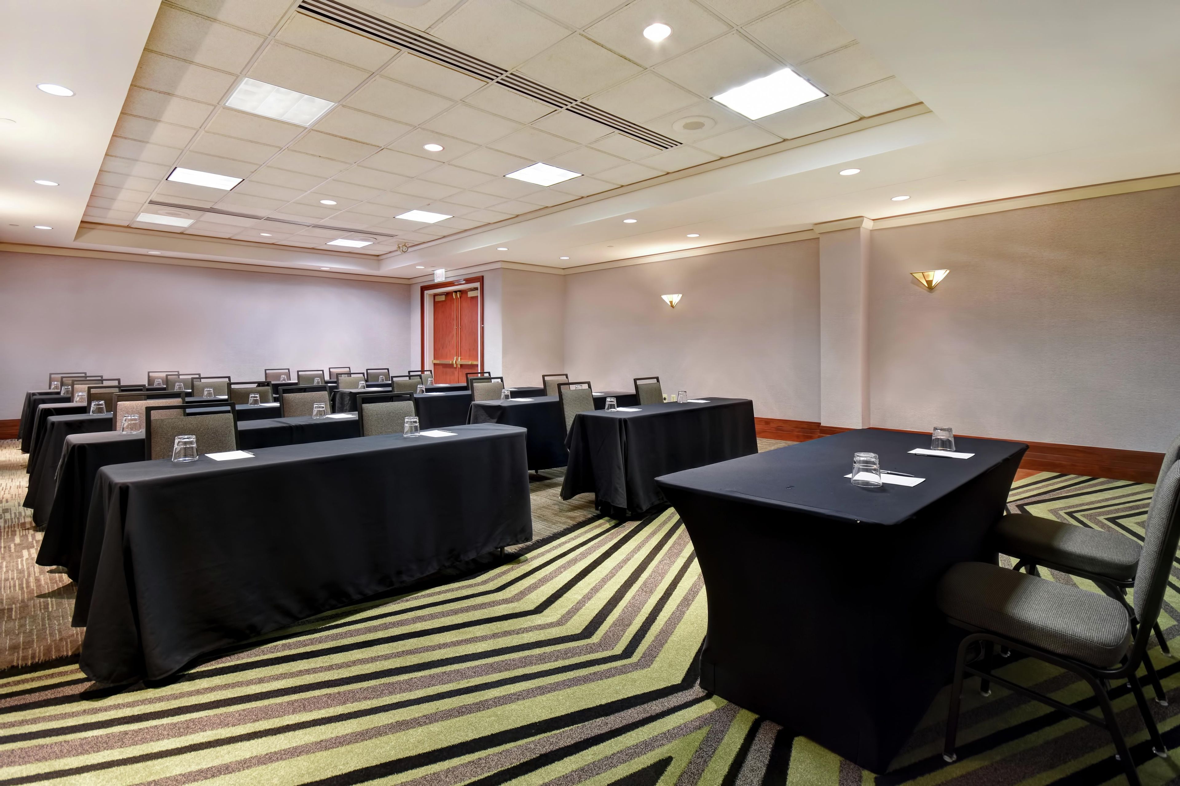 Sala de conferências com várias mesas e cadeiras, equipada com placas de identificação e copos d'água.