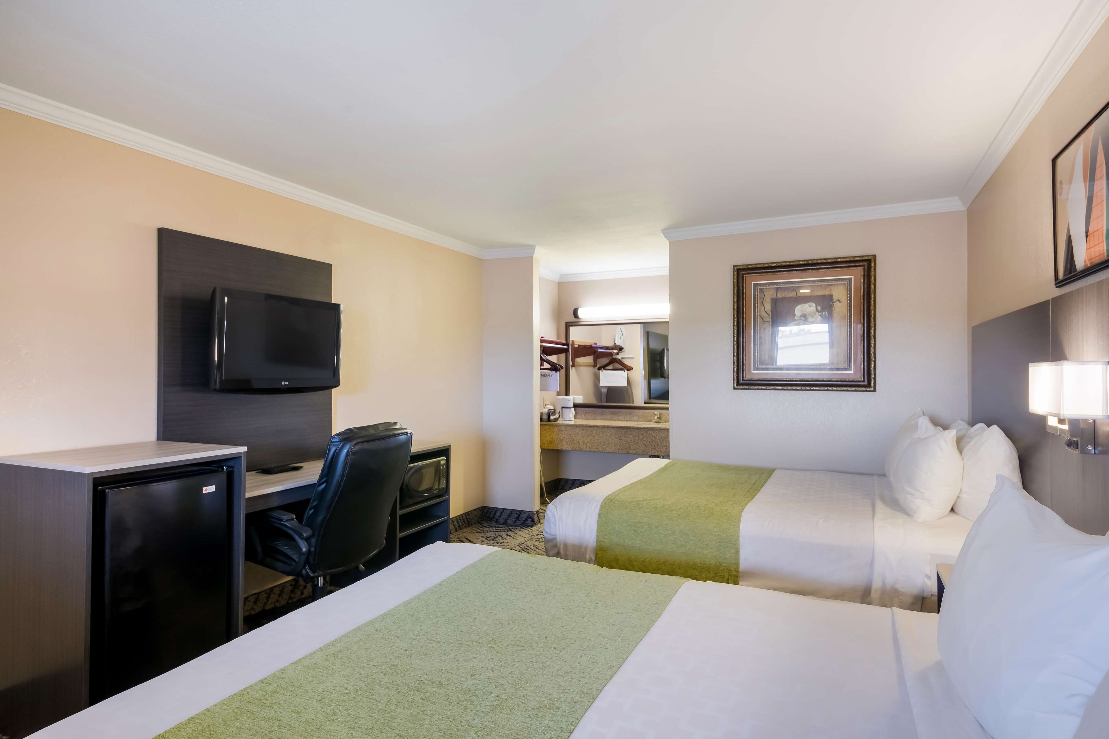 Quarto de hotel com duas camas, uma escrivaninha com computador, televisão e um pequeno frigorífico.