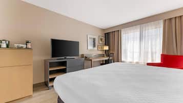 Quarto de hotel com cama, escrivaninha, televisão e cadeira.