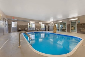 Piscina interior com água azul cristalina, rodeada por piso e paredes azulejadas, com uma escada de metal dando acesso à piscina.