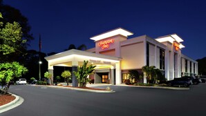 Um hotel Hampton Inn com design moderno, destacando uma entrada bem iluminada e um estacionamento.