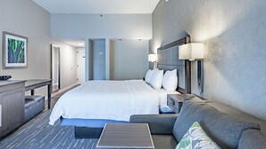 Quarto de hotel moderno com uma cama grande, um sofá, uma mesa pequena, uma escrivaninha e um abajur.