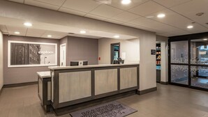 Uma área de recepção com balcão, uma moldura na parede e um tapete de entrada com mensagem.