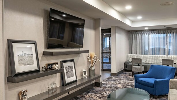 Quarto de hotel com televisão de tela plana na parede, um sofá, mesa de centro de vidro e carpete estampado.