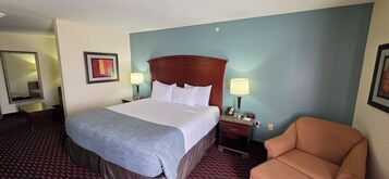 Quarto de hotel com uma cama grande, duas mesas de cabeceira com luminárias, uma cadeira e um espelho.