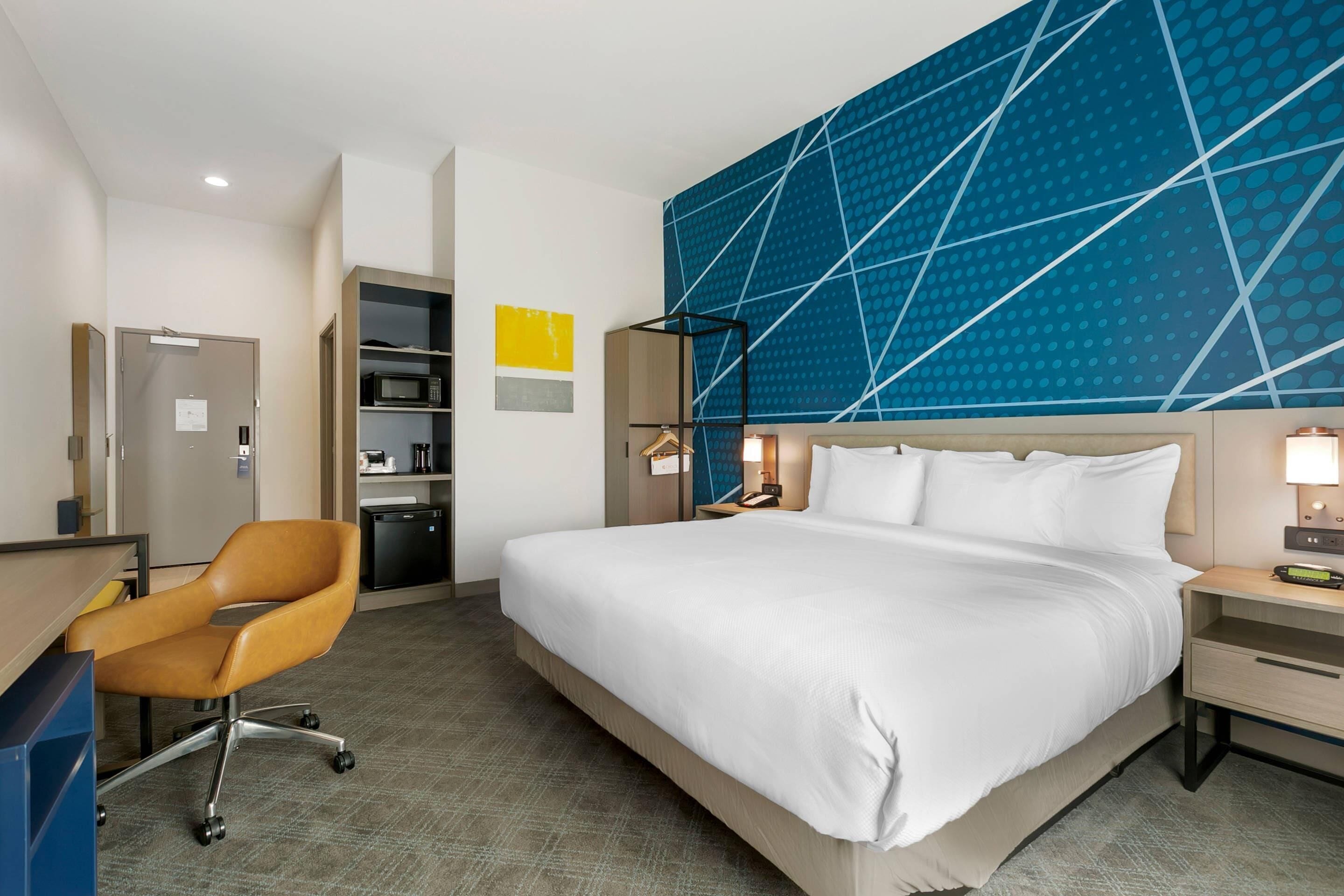 Quarto de hotel com uma cama grande, uma escrivaninha com cadeira, micro-ondas e guarda-roupa.