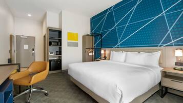 Quarto de hotel com uma cama grande, uma escrivaninha com cadeira, micro-ondas e guarda-roupa.