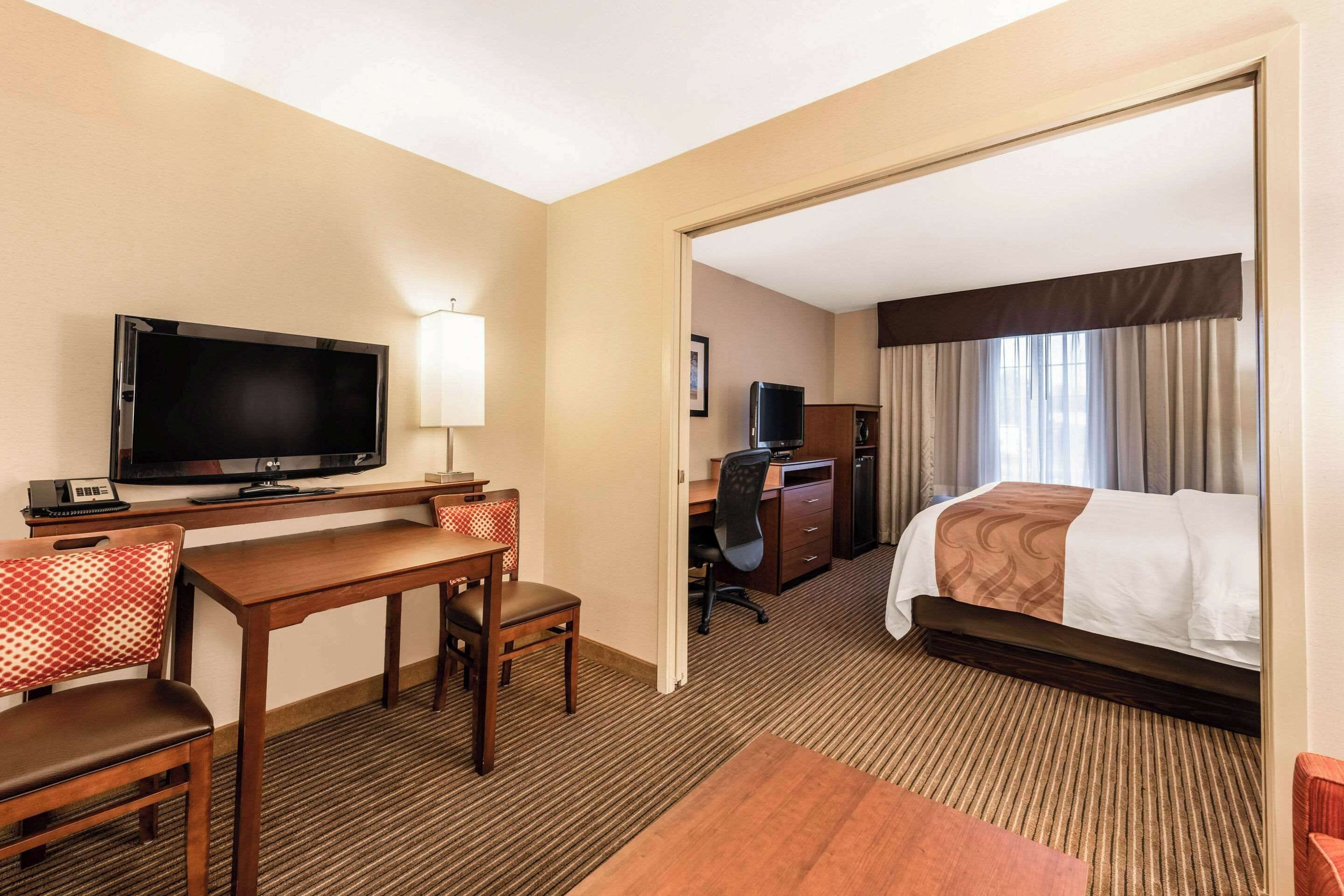 Quarto de hotel com uma cama, uma mesa com cadeira, uma televisão e uma luminária.