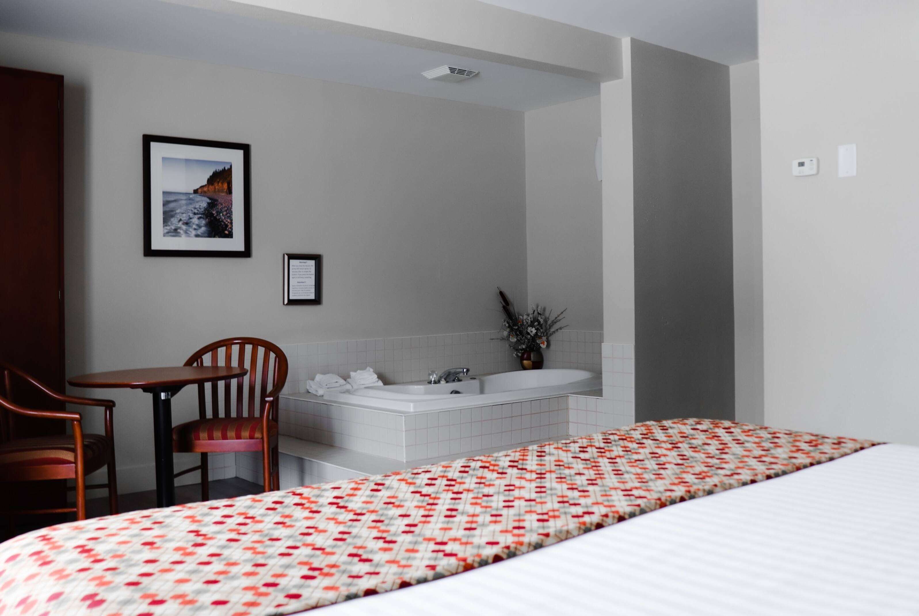 Quarto de hotel com uma cama, uma mesinha com cadeira, uma banheira e um quadro na parede.