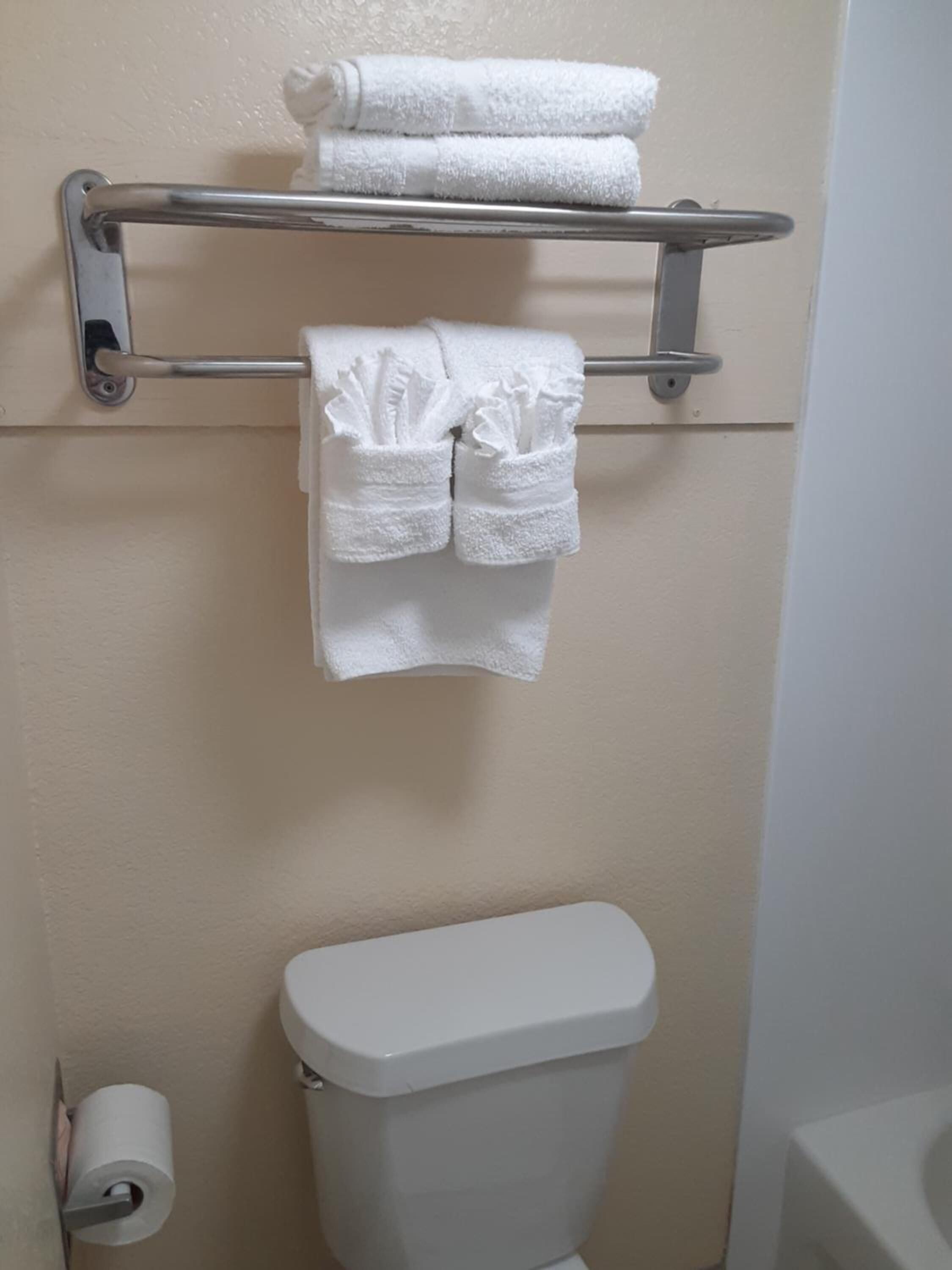 Uma casa de banho com sanita, um porta-toalhas com toalhas dobradas e um rolo de papel higiénico.
