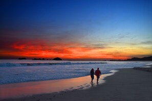 Cena de praia com duas pessoas caminhando pela orla durante o pôr do sol.