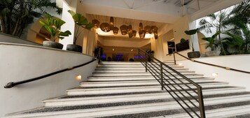 Escadaria com corrimão, conduzindo a um hall com luminária no teto e plantas em vasos.