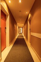 Corredor de hotel com piso carpeteado, portas em ambos os lados e iluminação embutida.