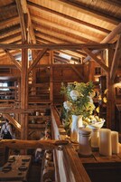 Interior rústico de madeira, com mesa de jantar posta, um vaso com flores e velas.