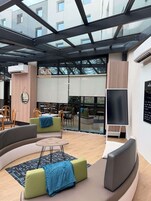 Uma área de estar moderna ao ar livre, com mobiliário acolchoado, teto de vidro e vista para a paisagem urbana.