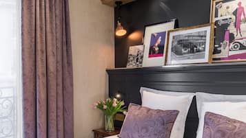 Cama bem arrumada com almofadas estampadas, mesa de cabeceira com um vaso de flores e parede com quadros.