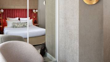 Quarto de hotel com cama, uma cadeira, mala e espelho fixado na parede.