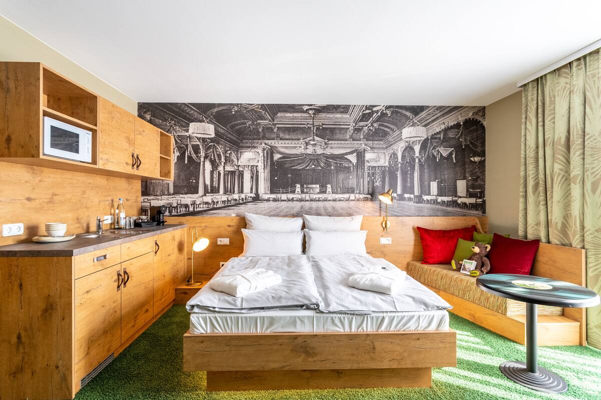 Quarto de hotel moderno com uma cama grande, armário de madeira e uma kitchenette.