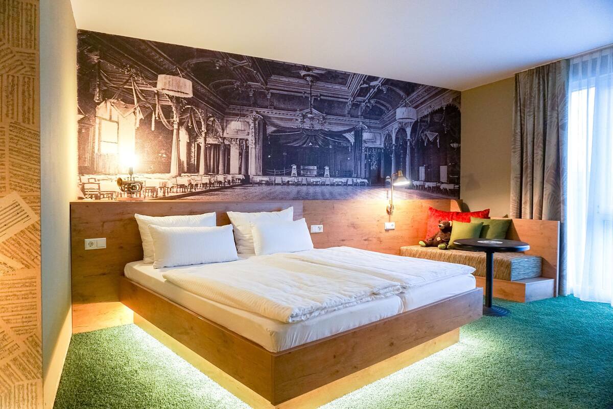 Quarto de hotel com uma cama grande, um mural na parede, uma mesinha e um sofá.