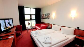 Quarto de hotel com duas camas, televisão, sofá vermelho, mesa pequena e janela com cortinas.