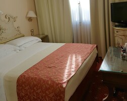 Quarto de hotel com cama, escrivaninha, televisão e cortinas.