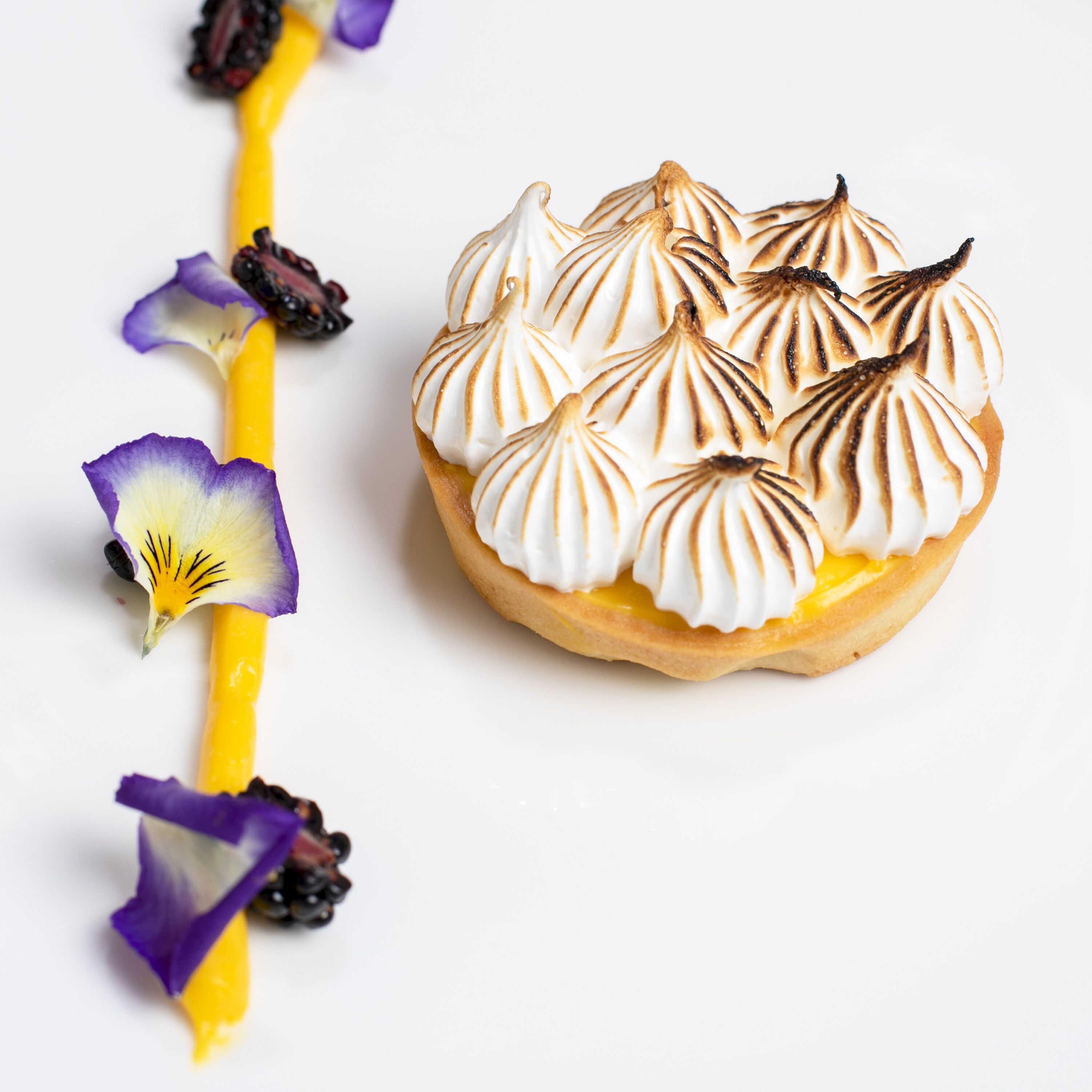 Uma sobremesa com cobertura de merengue, rodeada por flores amarelas e roxas.