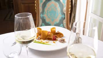Uma mesa de jantar com um prato de comida, dois copos de vinho e uma cadeira com encosto decorativo.