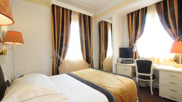 Quarto de hotel com cama, escrivaninha, cadeira e cortinas.