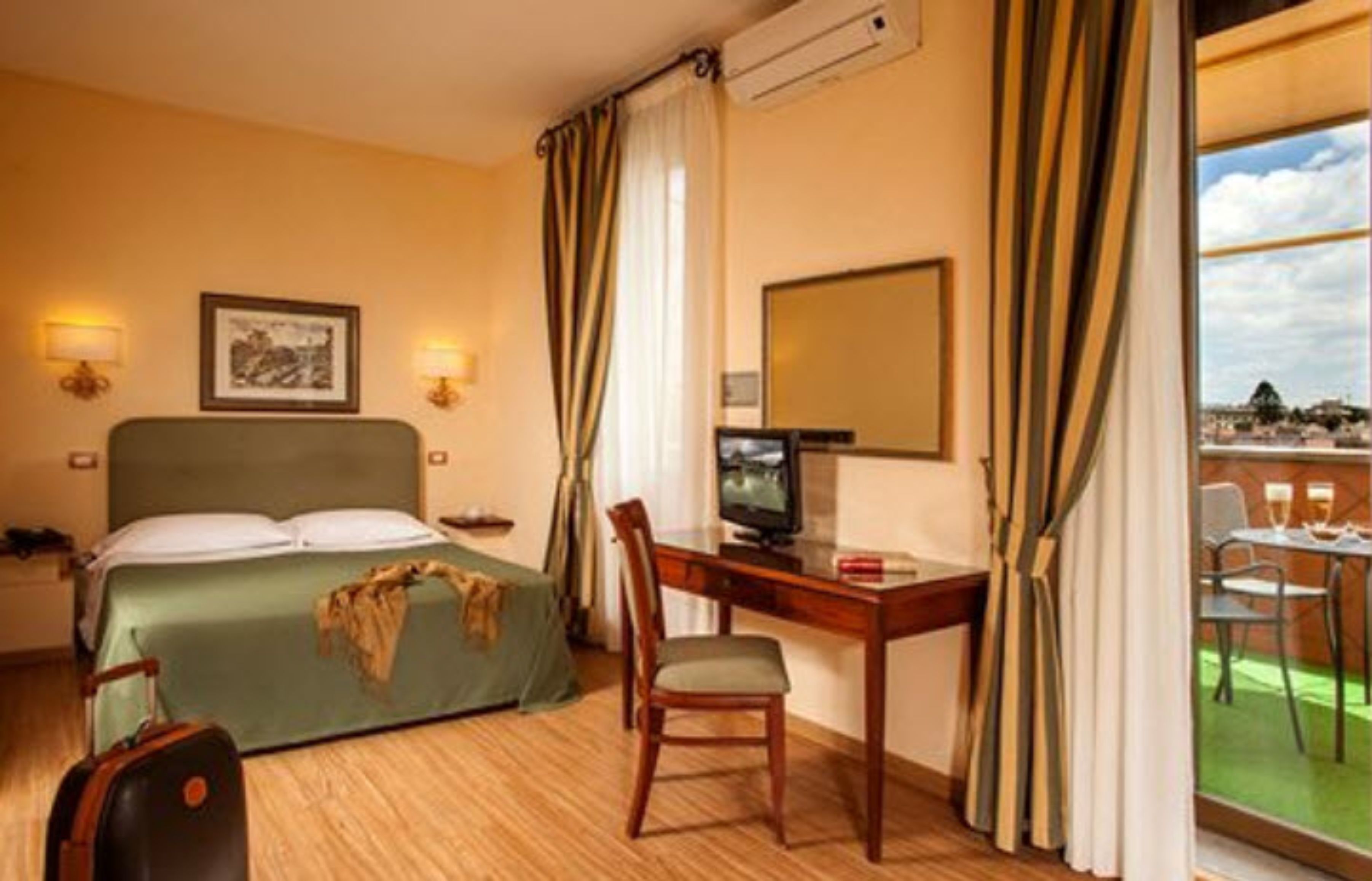 Quarto de hotel com cama, escrivaninha, cadeira, televisão e vista para a cidade pela janela.
