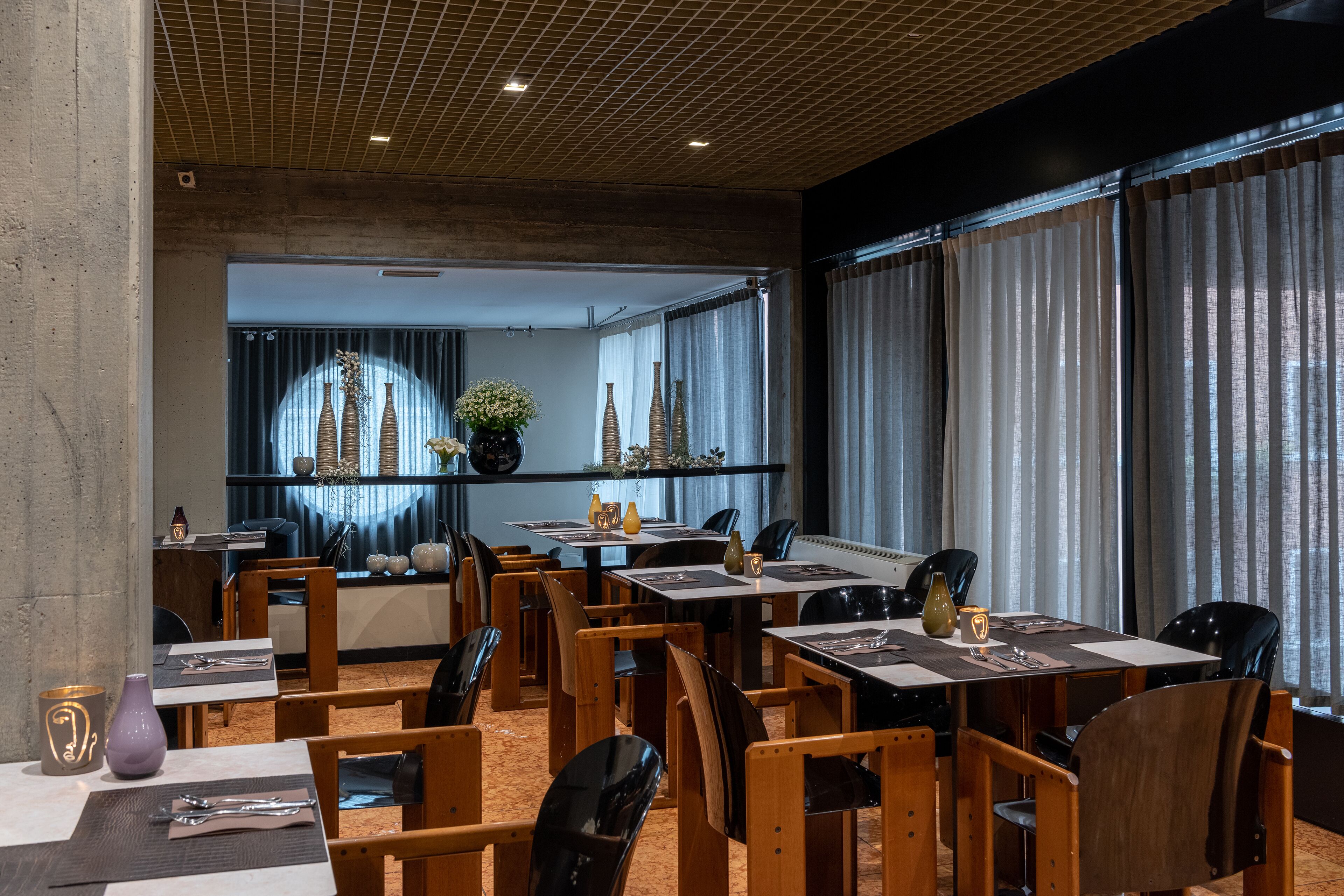 Uma sala de conferências com várias mesas e cadeiras, amplas janelas com cortinas e um design de teto moderno.