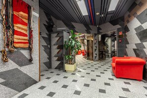 Um hall com chão quadriculado, um sofá vermelho e um vaso de planta.