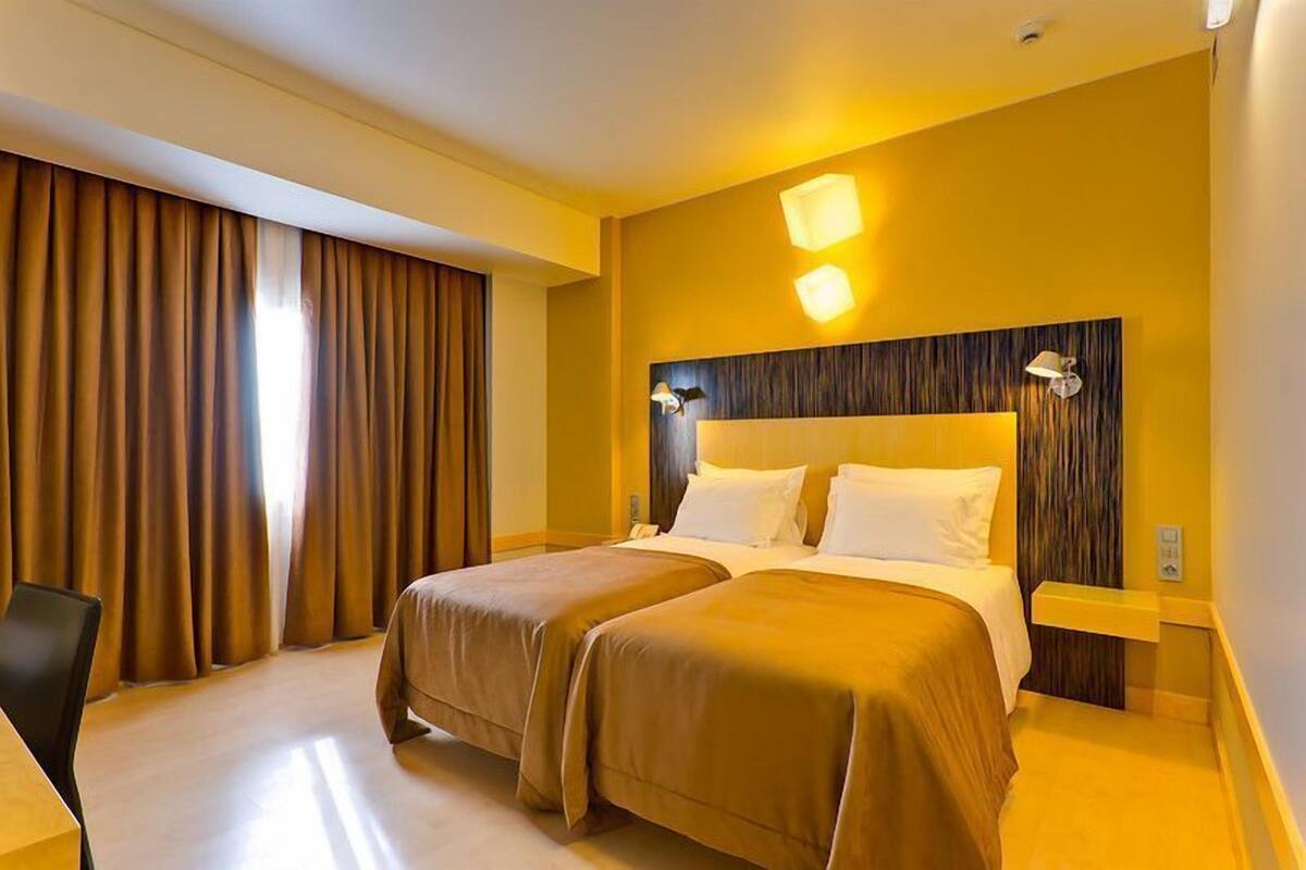 Quarto de hotel com duas camas, uma escrivaninha e uma janela grande com cortinas.