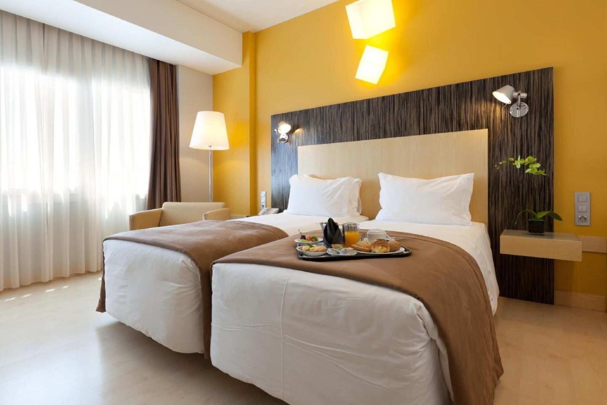 Quarto de hotel com duas camas, uma mesinha de cabeceira, um abajur e um tabuleiro com itens de café da manhã.