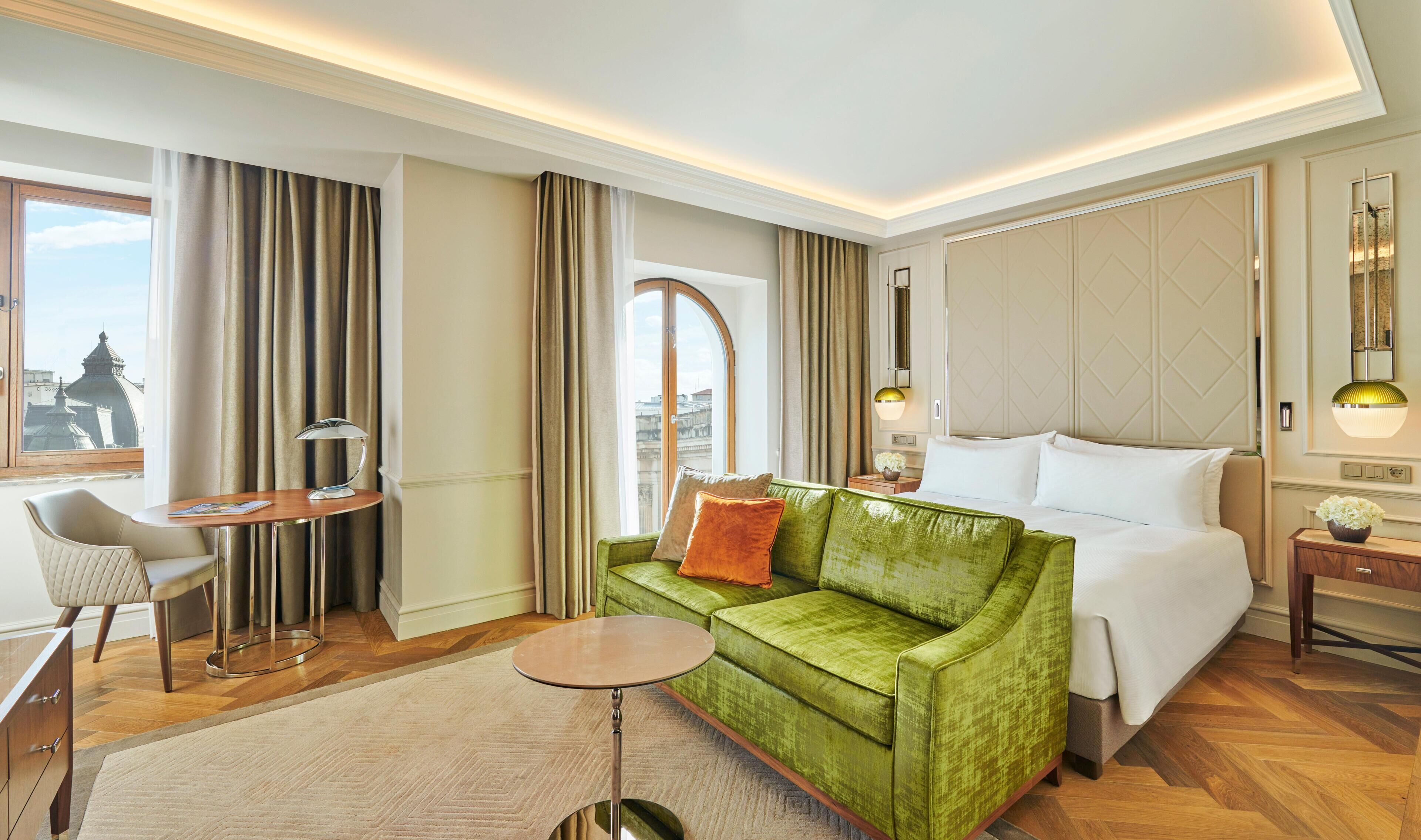 Quarto de hotel com sofá verde, uma cama, escrivaninha e uma cadeira.