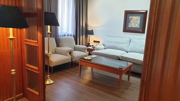 Sala de estar com sofá, poltrona e mesa de centro. Há duas luminárias, um quadro emoldurado na parede e piso de madeira.