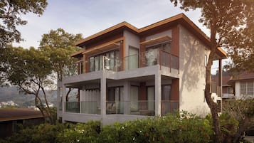 Uma casa moderna de dois andares com amplas janelas de vidro e varandas, cercada por vegetação exuberante.